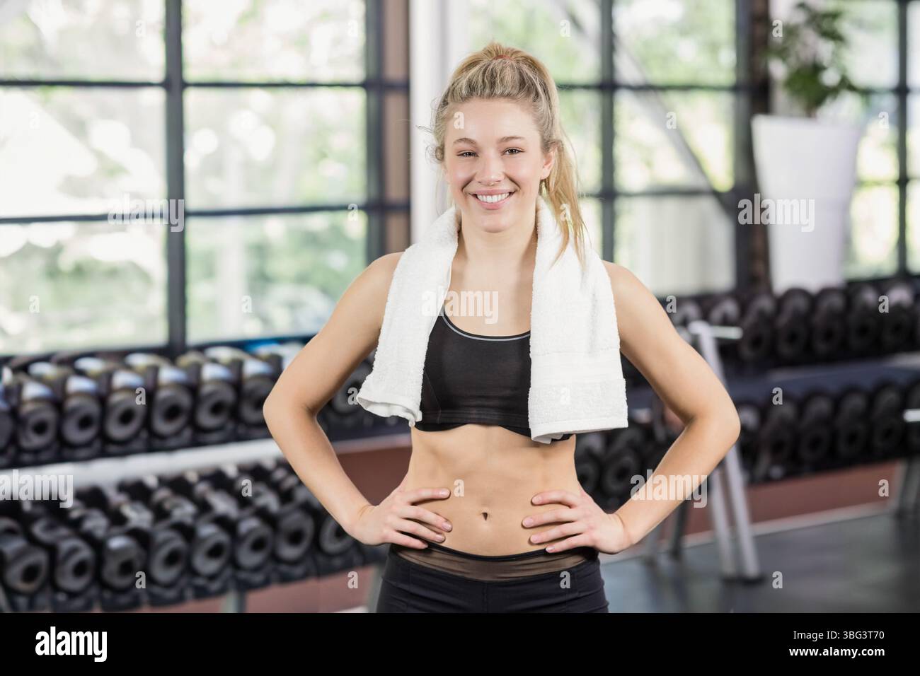 Female gym-goer standing confidently by rack of dumbbells near grid ...