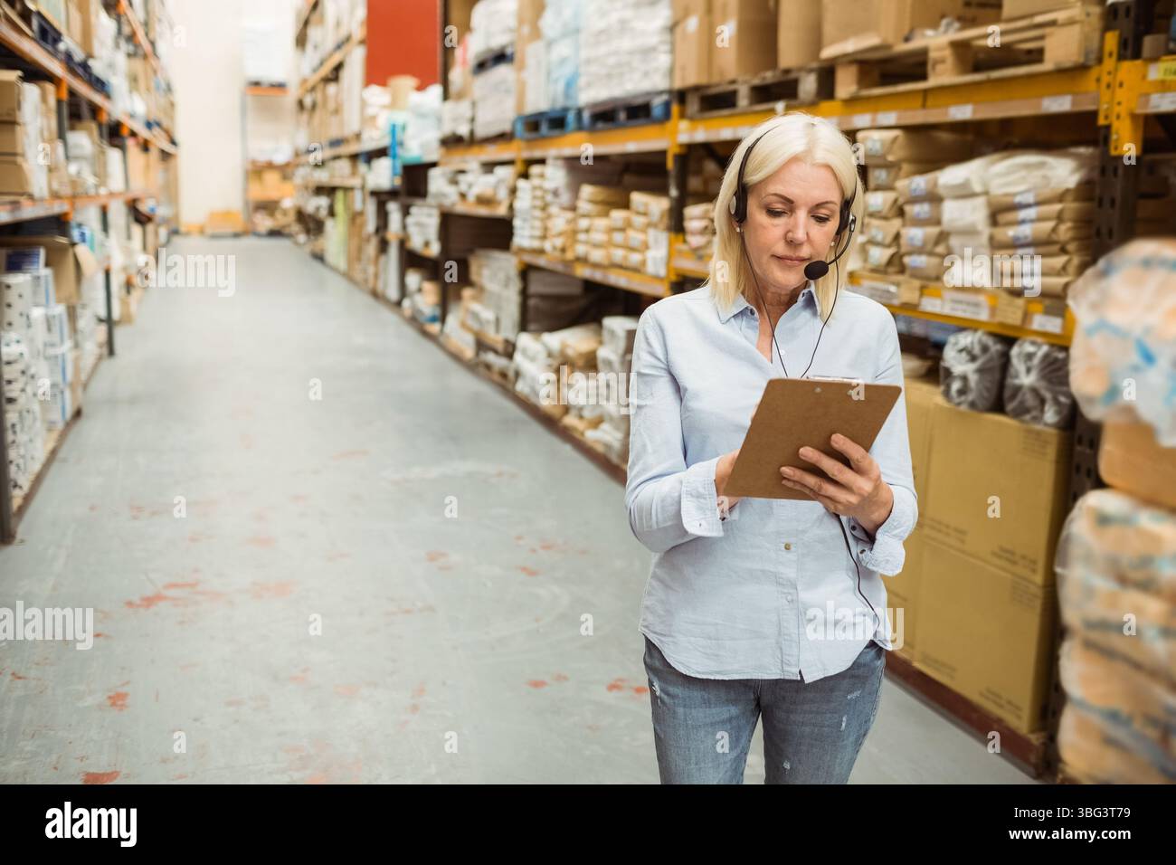 Woman standing in warehouse aisle scanning inventory on clipboard and ...