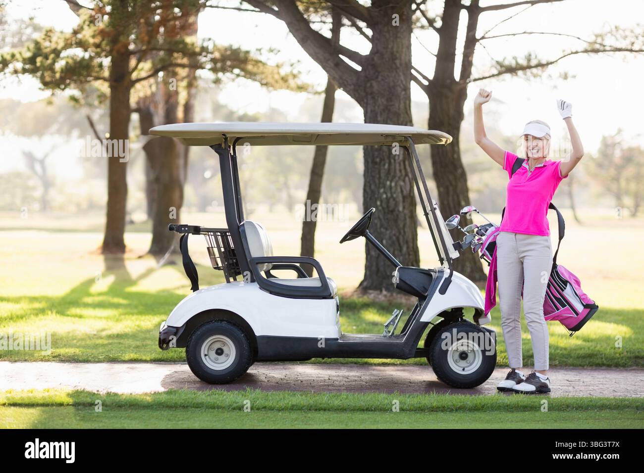 Woman in pink polo celebrating beside cart and clubs on golf course ...