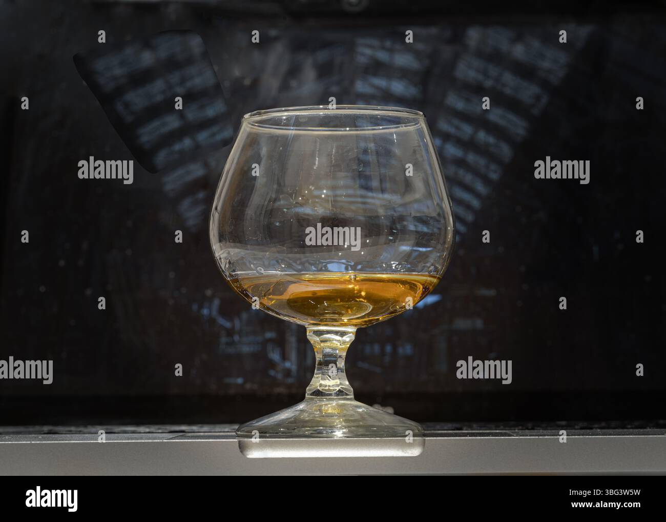 Whiskey glass or Brandy snifter stands on Laptop with laptop screen in ...
