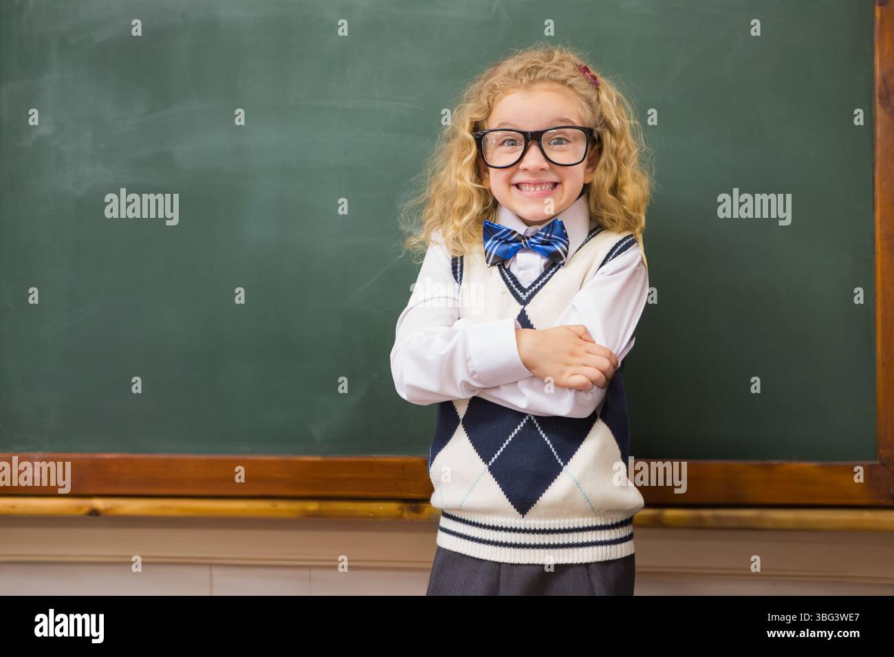 Female child student standing arms crossed by chalkboard, wearing ...