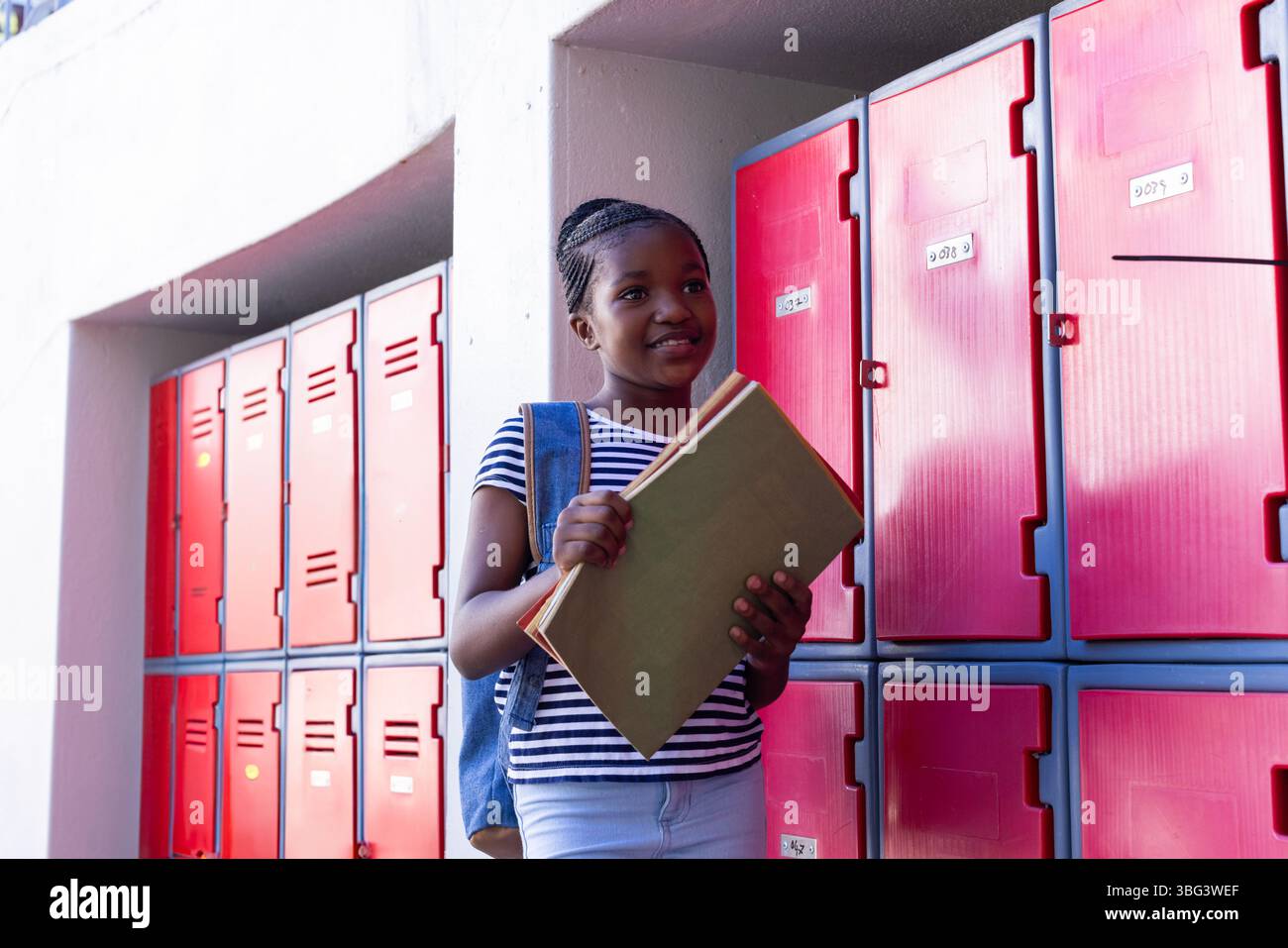 African American child holding green folder passing red lockers in ...