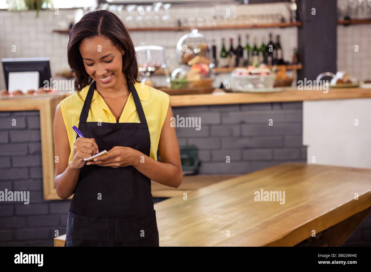 African American woman in apron standing behind cafe counter writing on ...