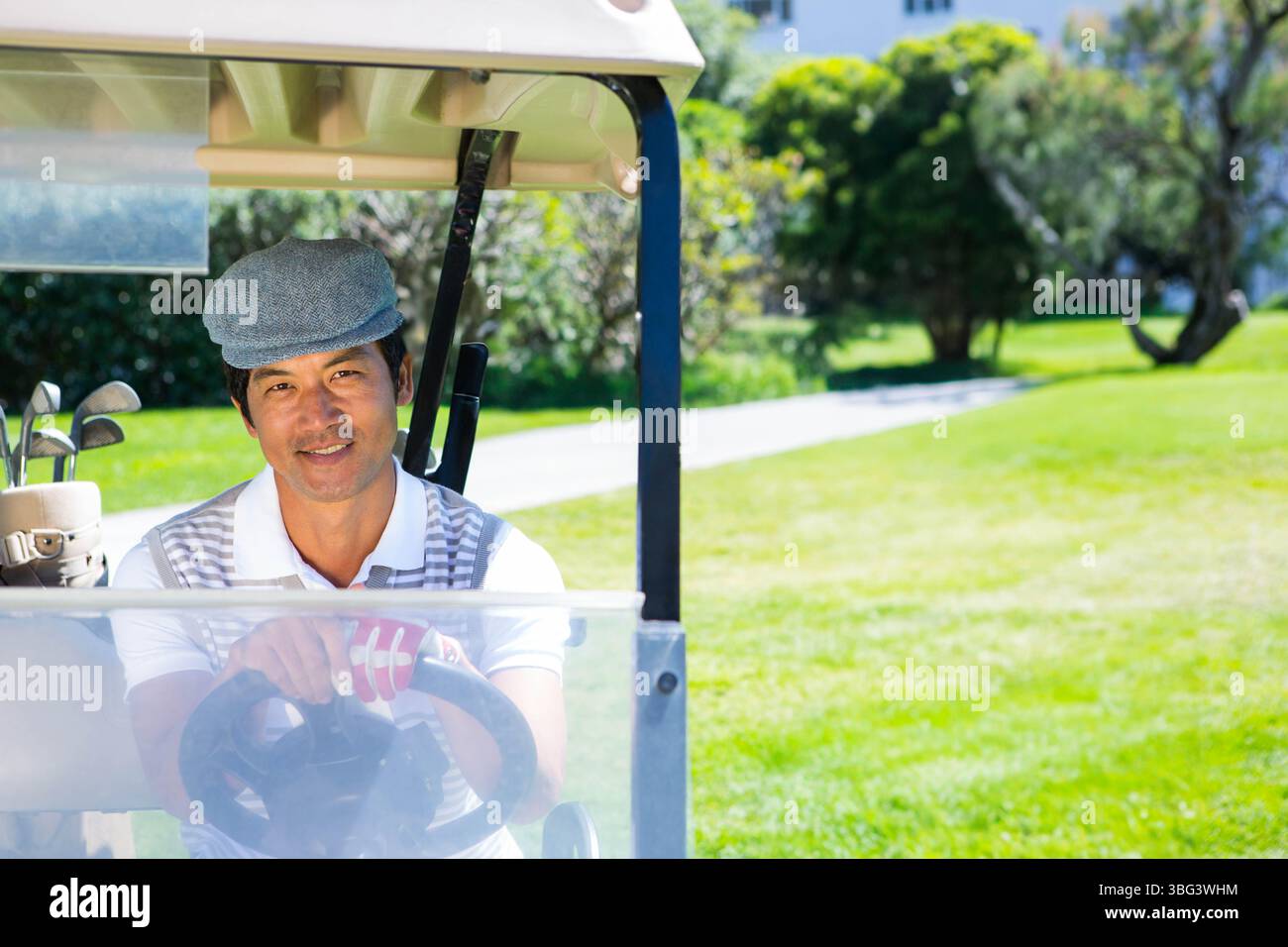Asian man driving golf cart on golf course with golf bag wearing flat ...