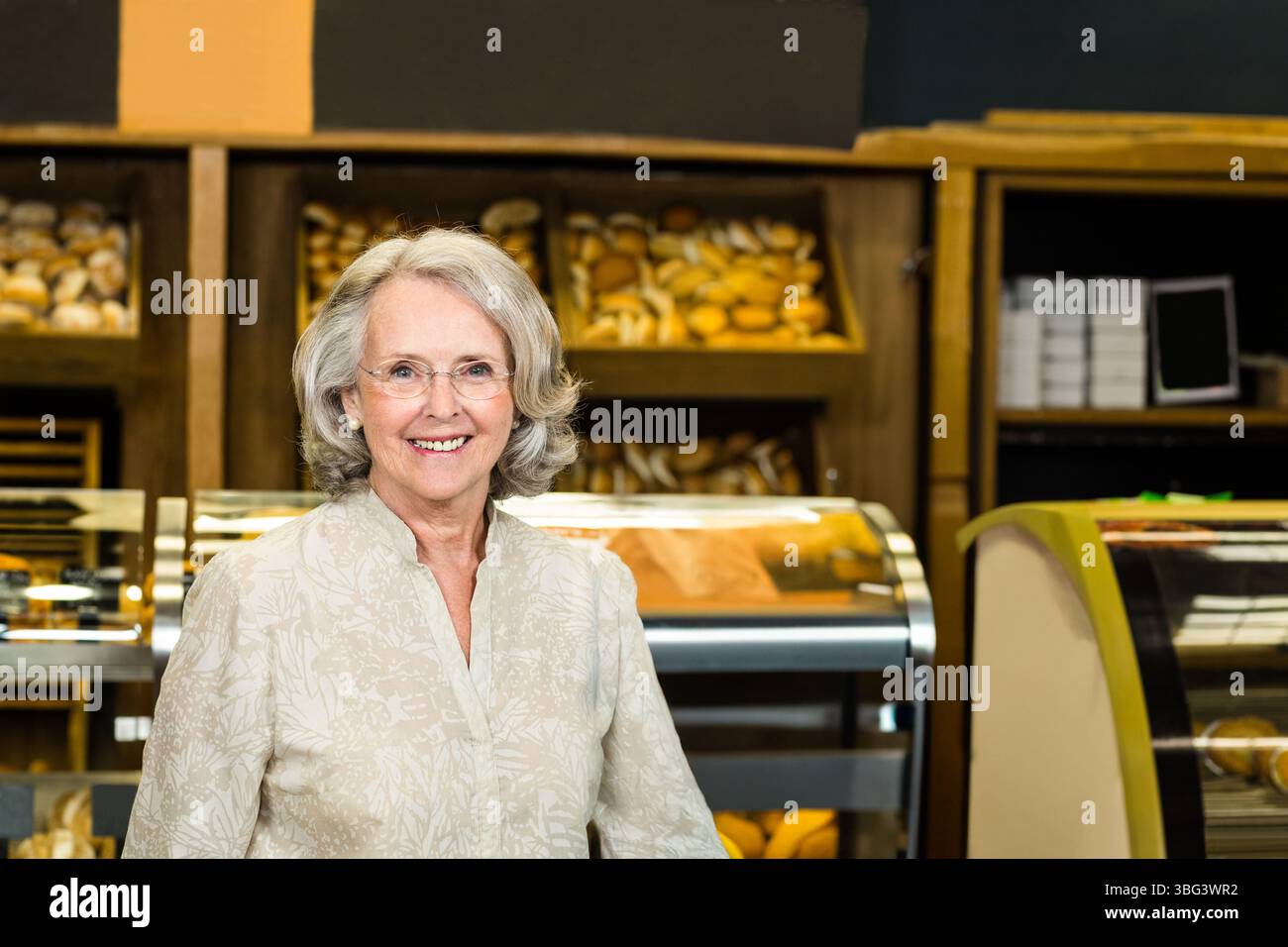 Senior woman standing behind bakery counter showcasing assorted ...