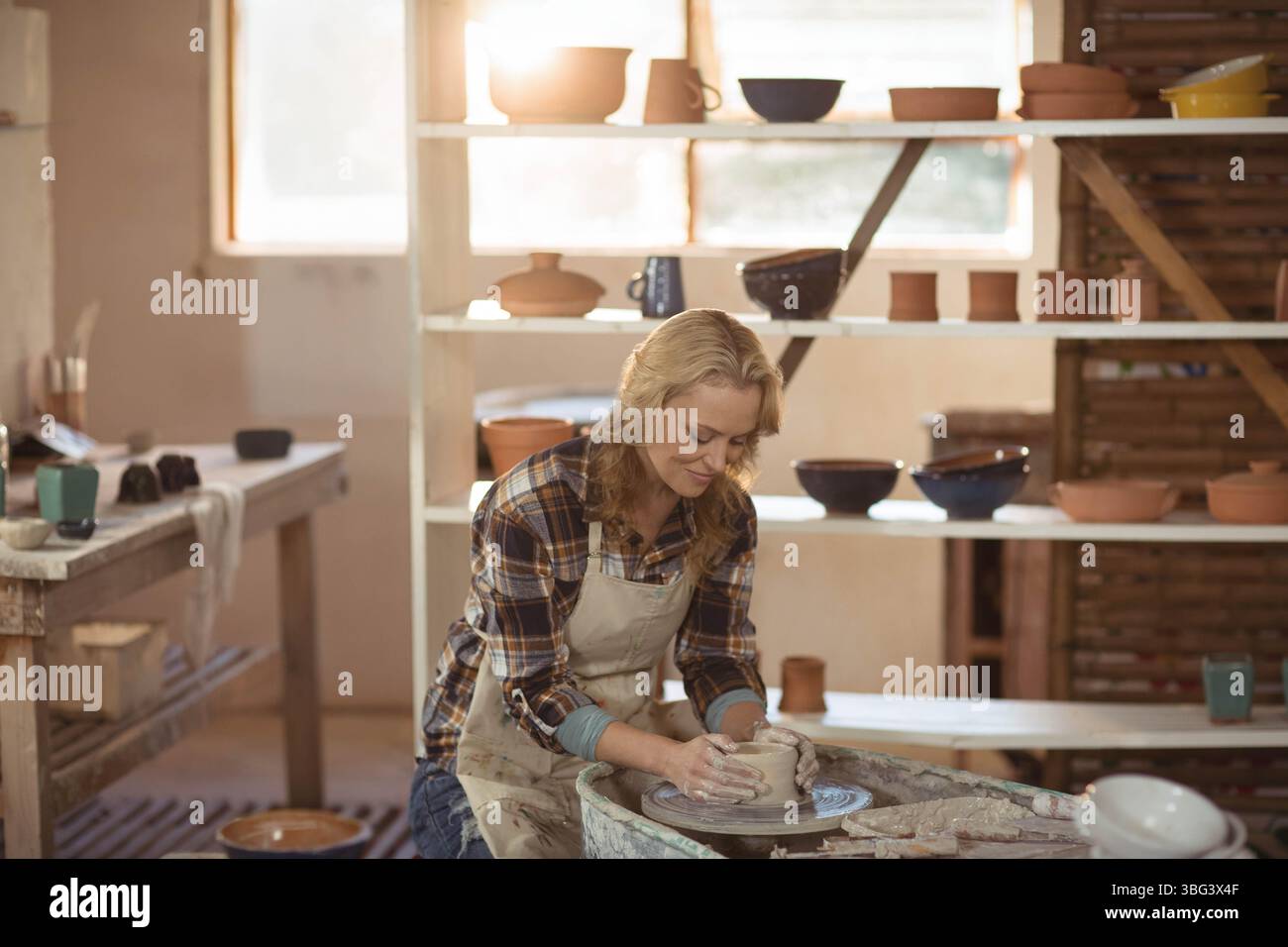 Pottery wheel spinning wet clay into vessel in sunlit workshop with ...