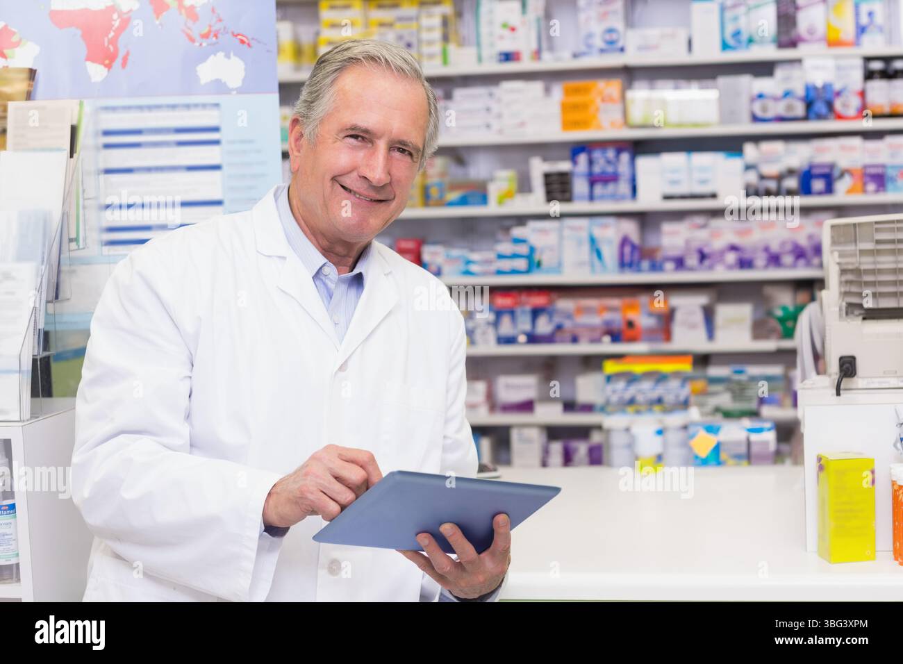Senior male pharmacist using tablet behind pharmacy counter with ...