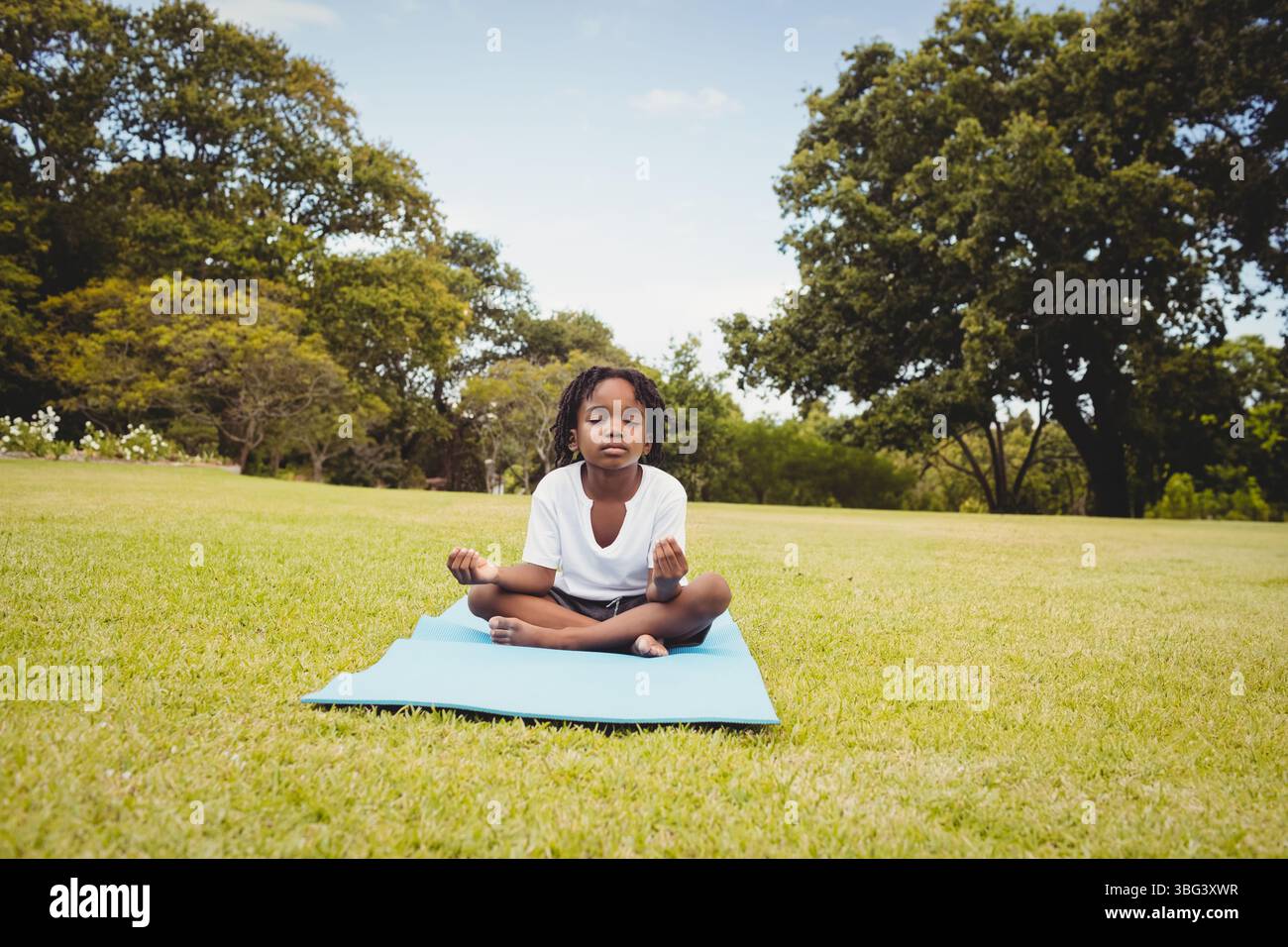 African American boy sitting cross-legged on blue yoga mat on green ...