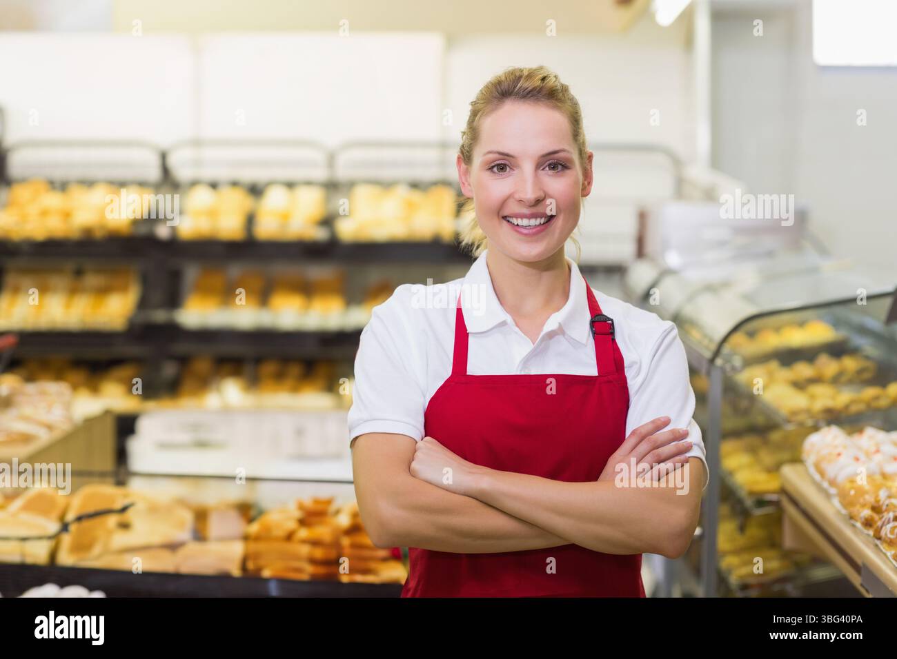 Woman in twenties wearing red apron standing behind counter in bakery ...