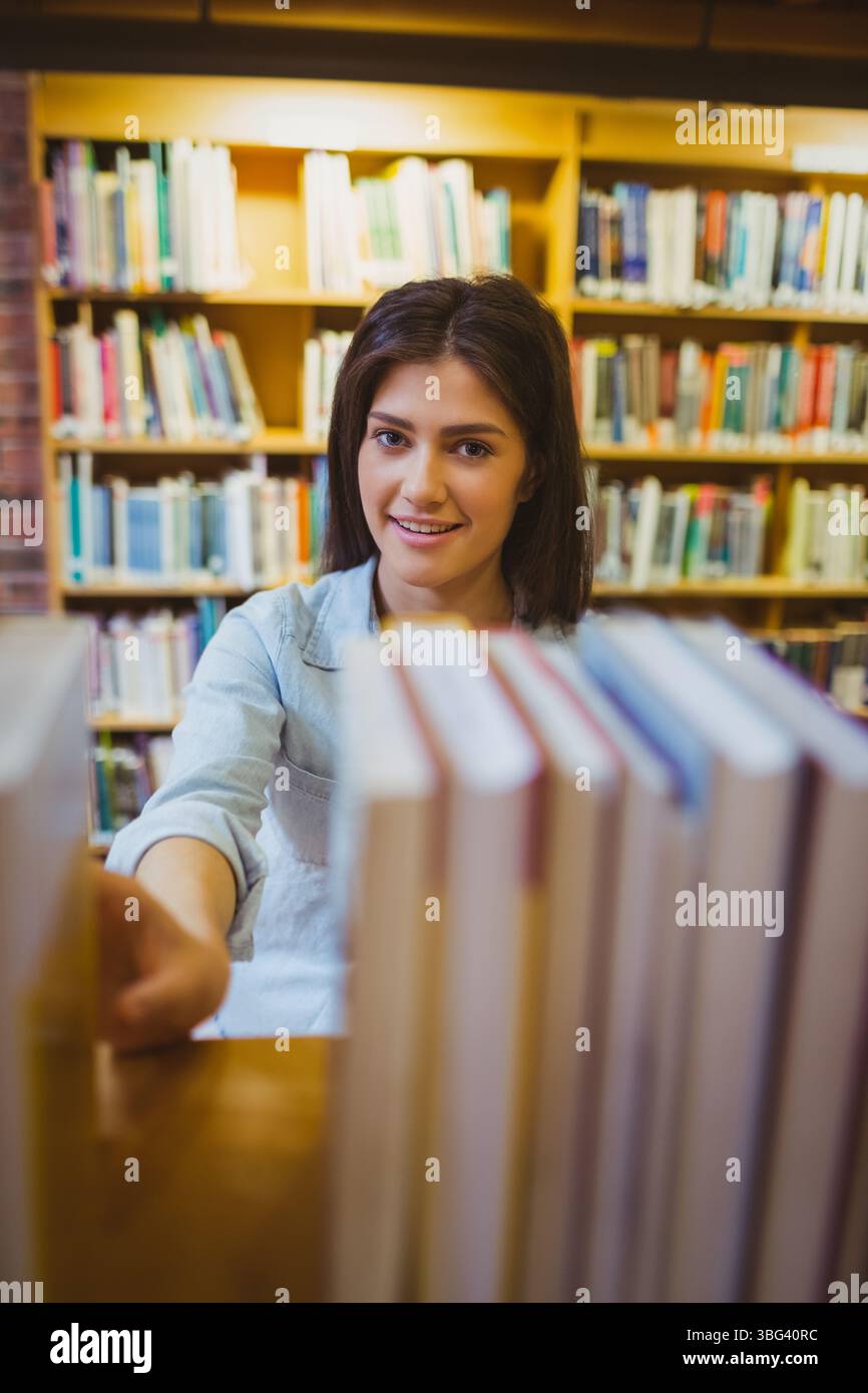Female student sitting at library reading area reaching for book on ...