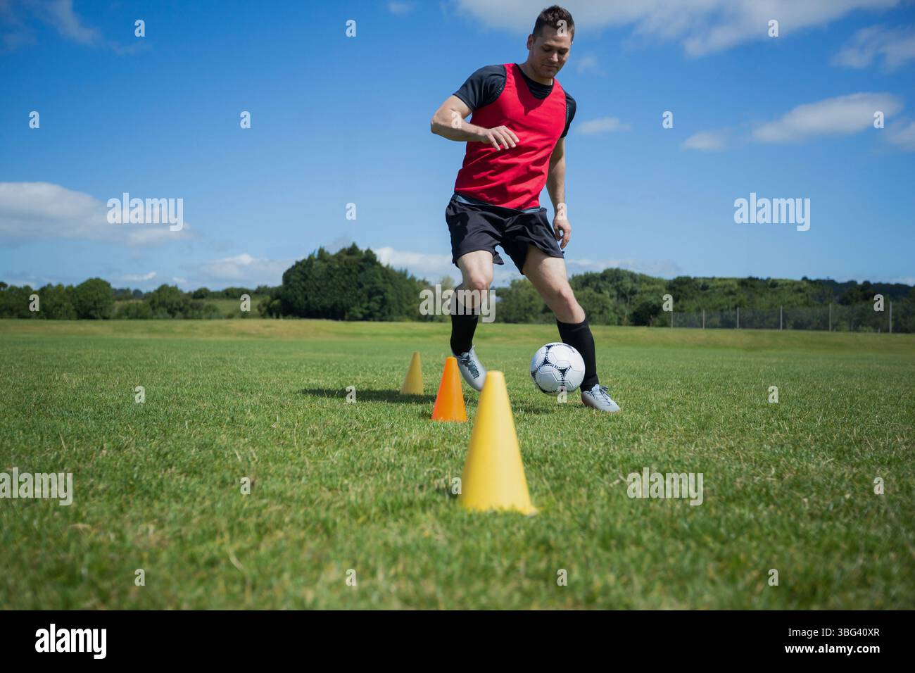Male athlete dribbling soccer ball around training cones on grass field ...