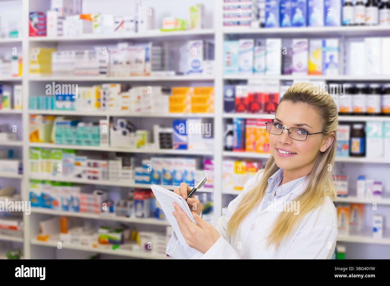 Female pharmacist wearing lab coat holding notepad and checking shelves ...