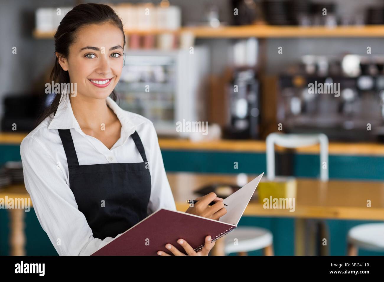 Female barista holding pen over notebook behind wooden counter at ...