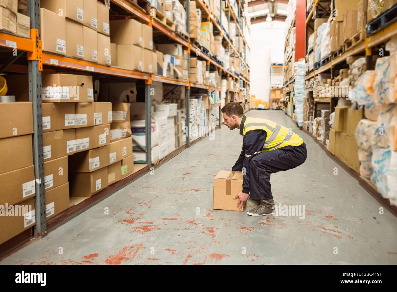 Male worker wearing high-visibility vest crouching and lifting ...
