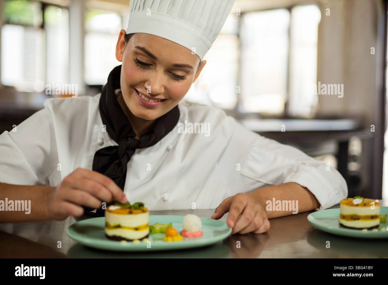 Female chef wearing white uniform at pastry station plating layered ...