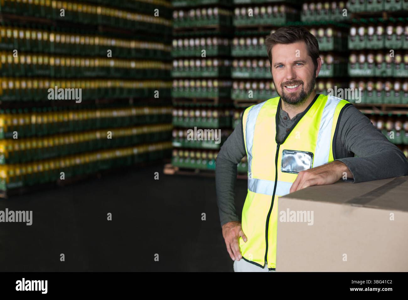 Man leaning on cardboard box in warehouse, wearing hi-vis safety vest ...