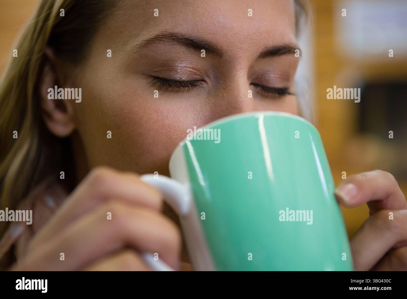Woman sipping from light green mug inside coffee shop with wooden ...