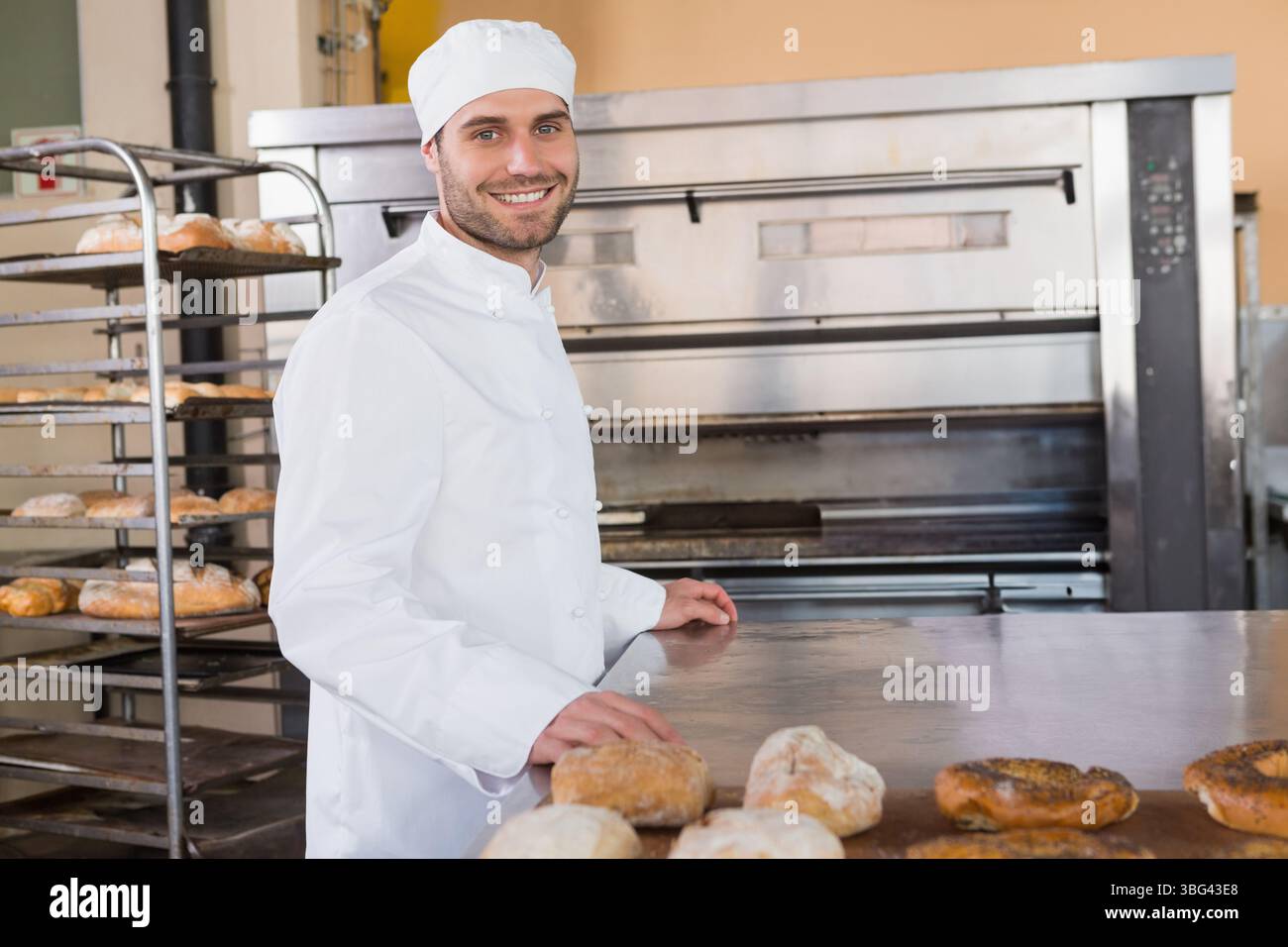Male baker wearing chef coat smiling while holding fresh loaf behind ...