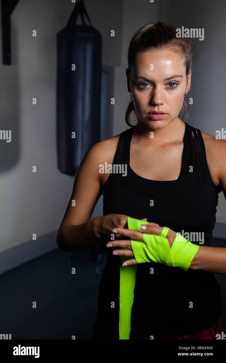 Woman wrapping bright green hand wraps on knuckles beside punching bag ...