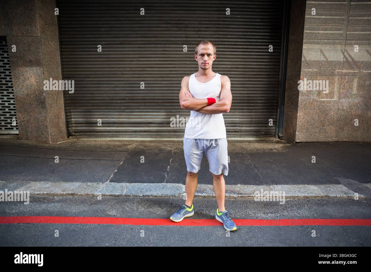 Man wearing athletic clothing standing with arms crossed behind red ...