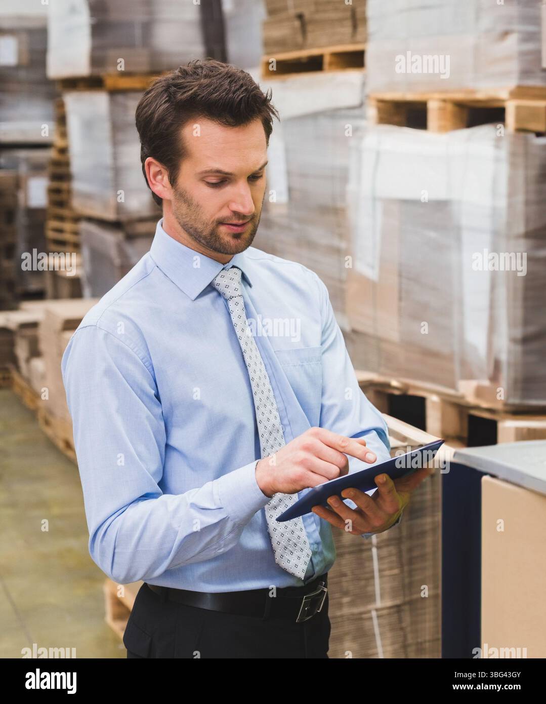 Male supervisor in shirt and tie reviewing inventory on tablet at ...