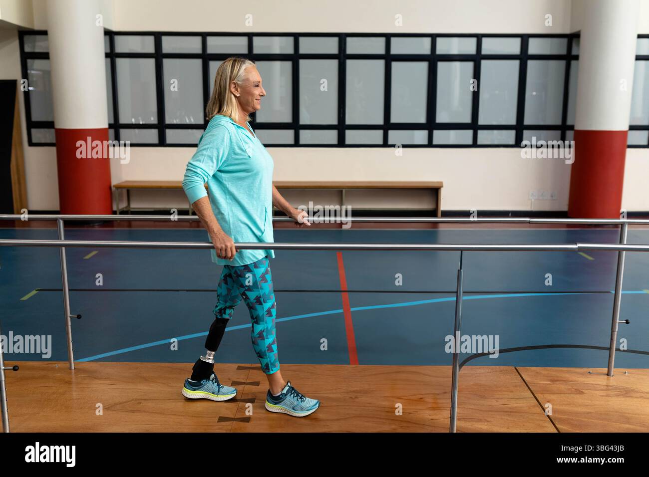 Senior woman walking in gym using parallel bars with prosthetic leg and ...