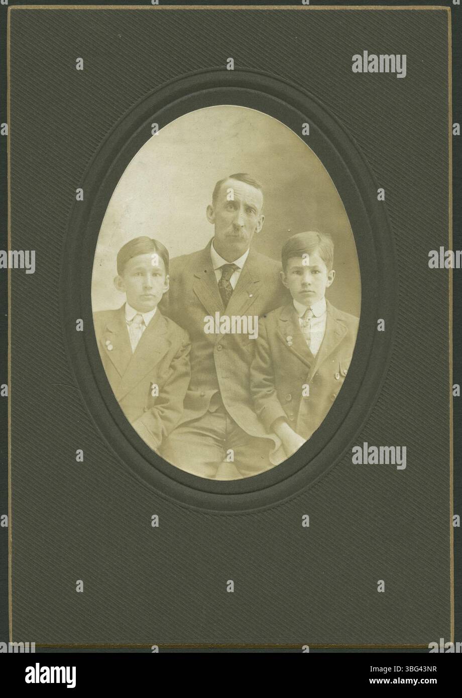 Group studio portrait of a seated man and two standing boys, all ...