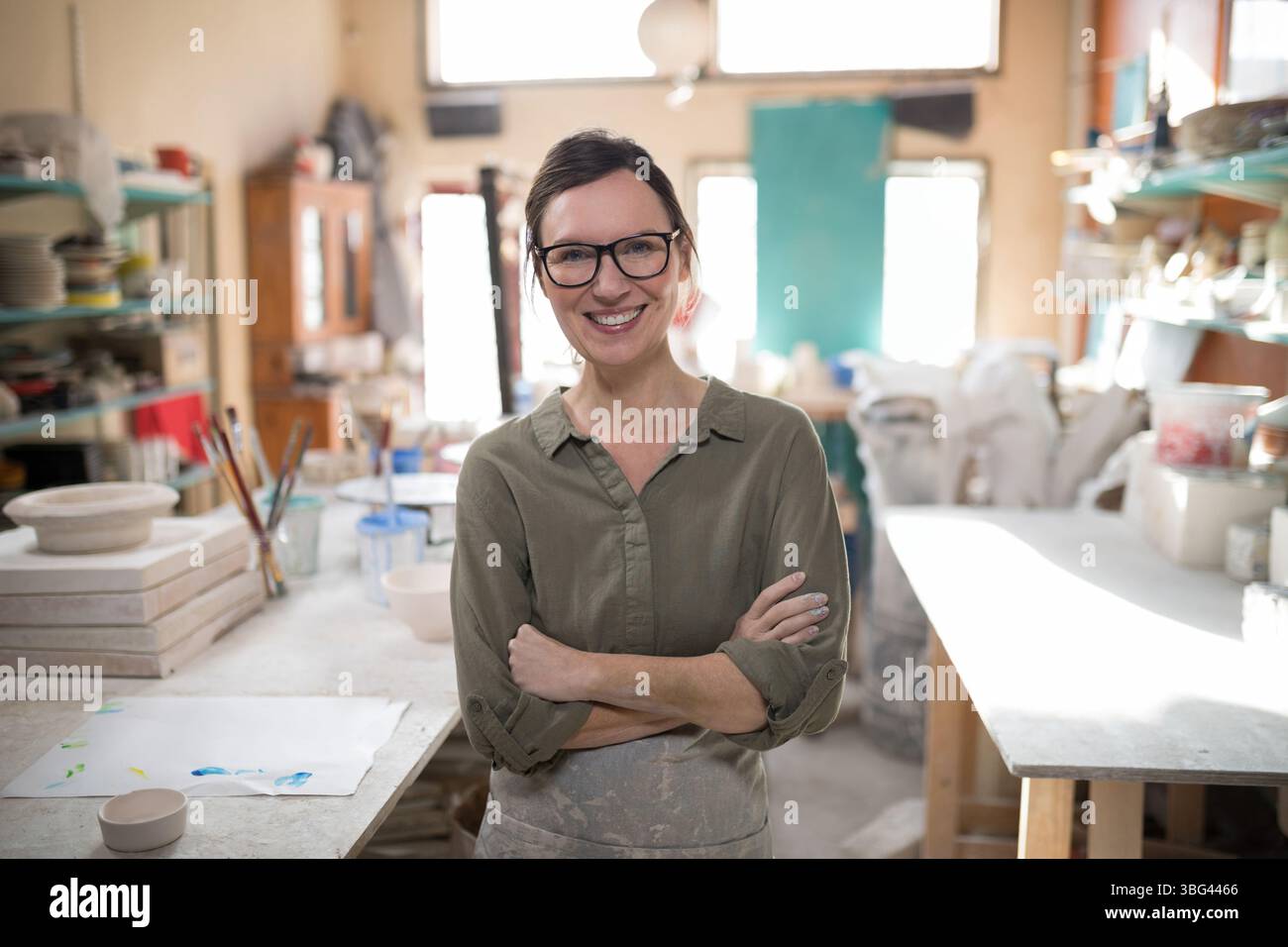 Female potter wearing clay-stained apron standing in pottery studio ...