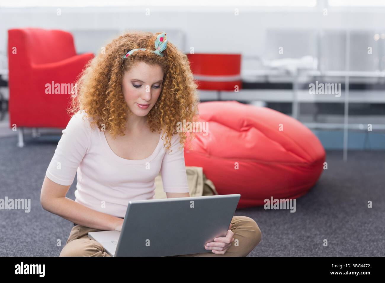Female student typing on laptop with backpack at side while sitting on ...