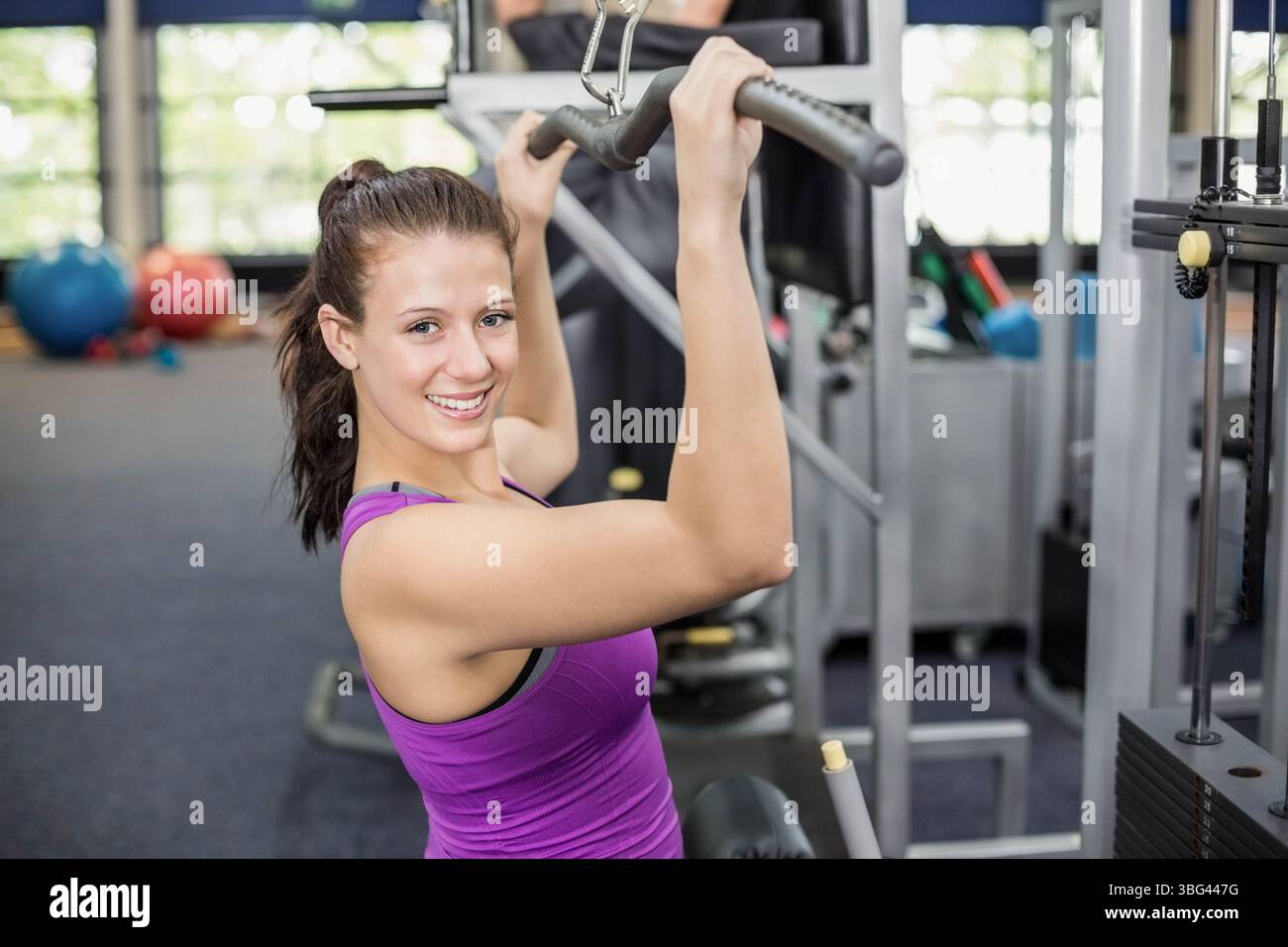 Woman performing lat pulldown exercise at gym in purple tank top using ...