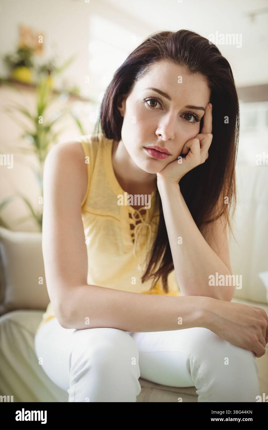 Woman sitting on sofa with pillow beside window and plant in living ...