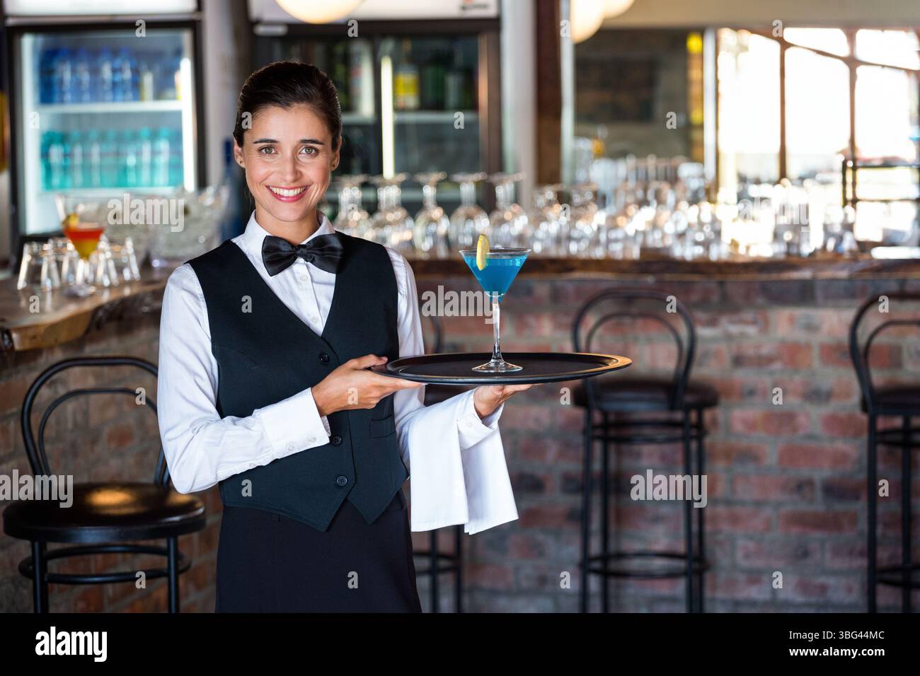 Female server holding blue cocktail on tray with lemon slice in brick ...