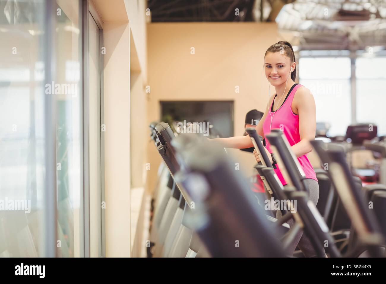 Woman running on treadmill near windows at fitness center wearing ...