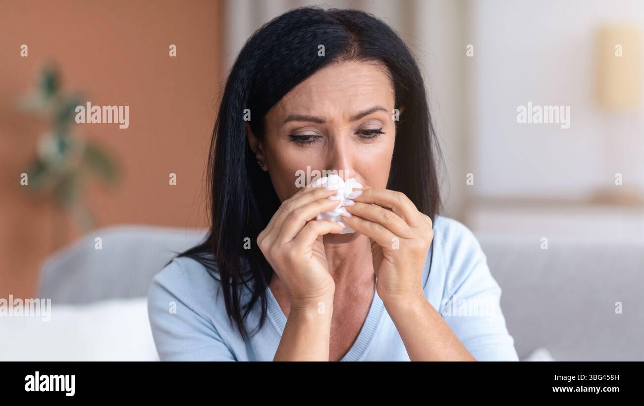 Sick mature woman sneezing and crying, holding tissue paper Stock Photo ...