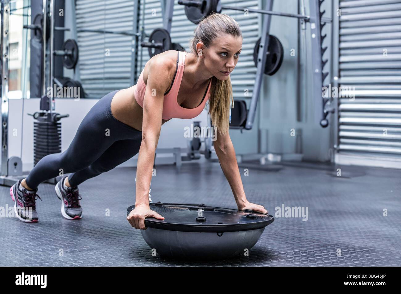 Woman performing plank push-up on BOSU ball in gym with rubber flooring ...