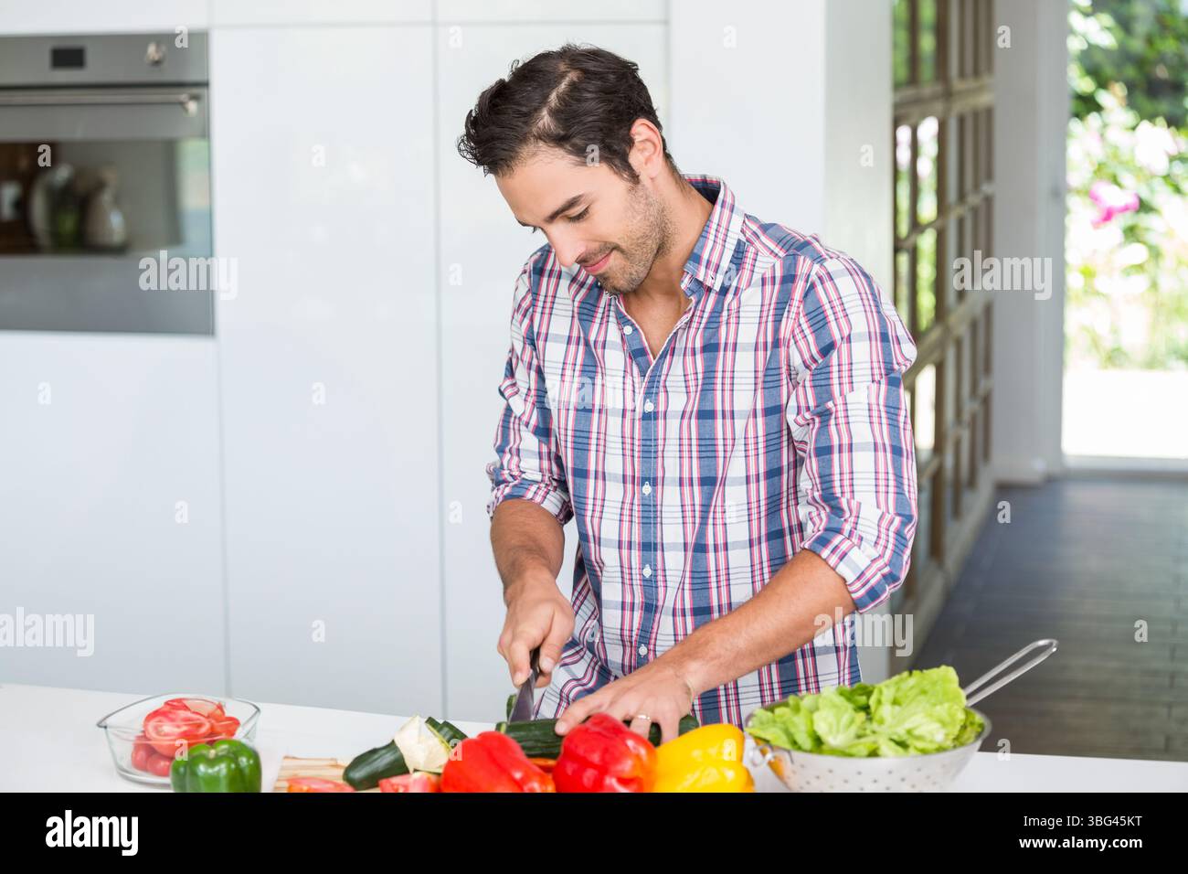 Man slicing zucchini with knife on counter in home kitchen with bell ...