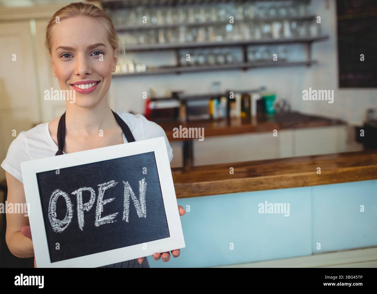 Woman holding OPEN chalkboard sign behind cafe counter with coffee ...