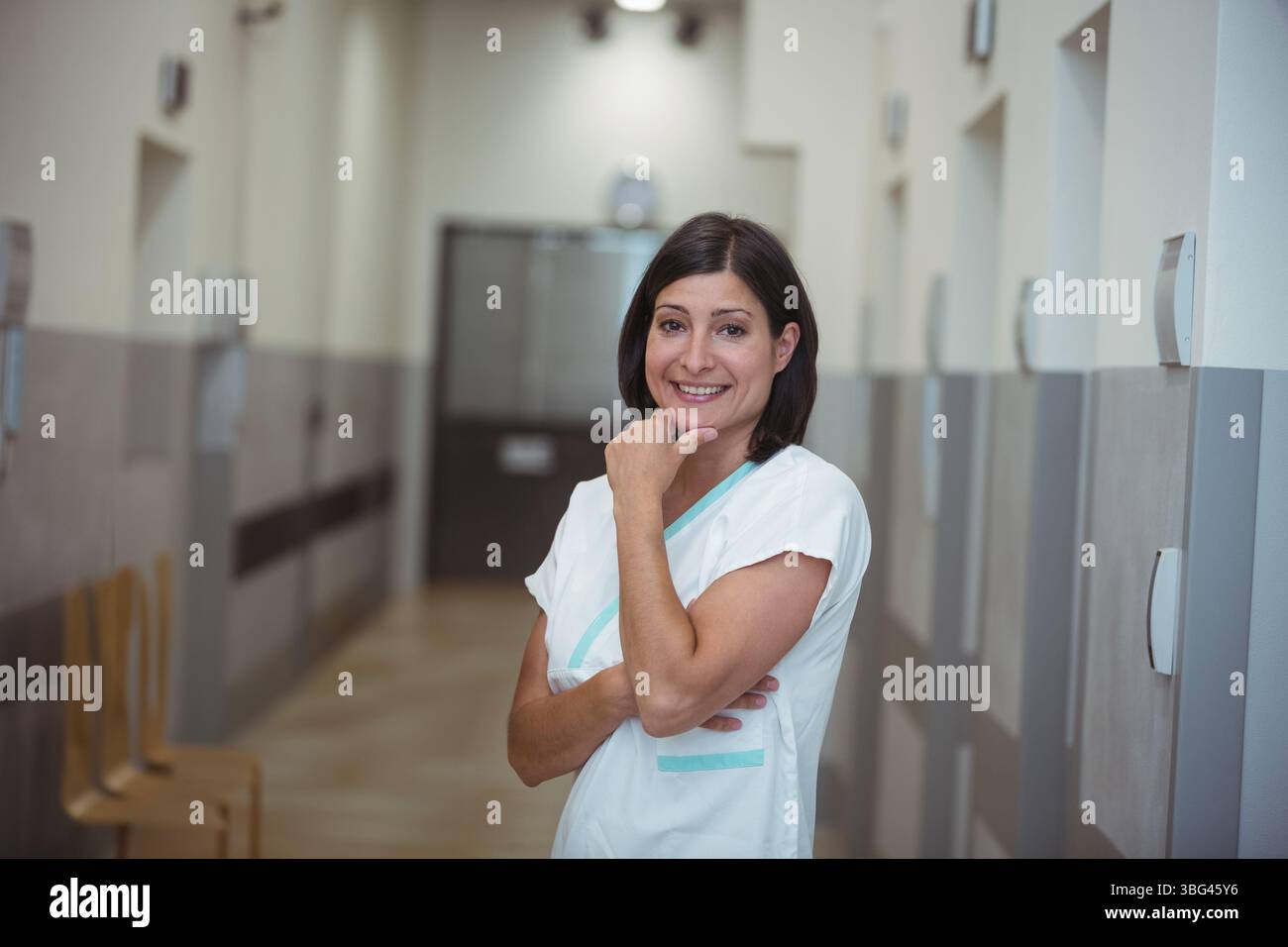 Female nurse standing and smiling in hospital corridor with wooden ...