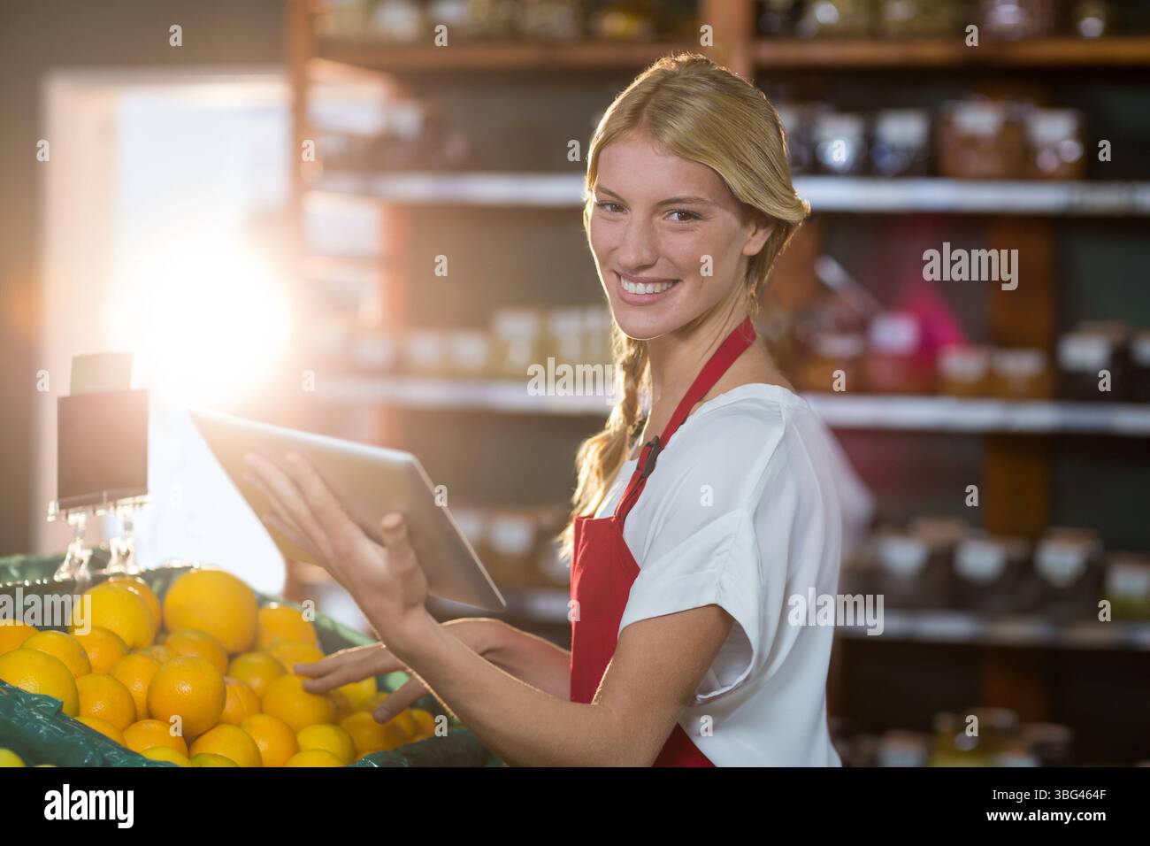 Woman produce clerk holding tablet and standing beside green orange ...