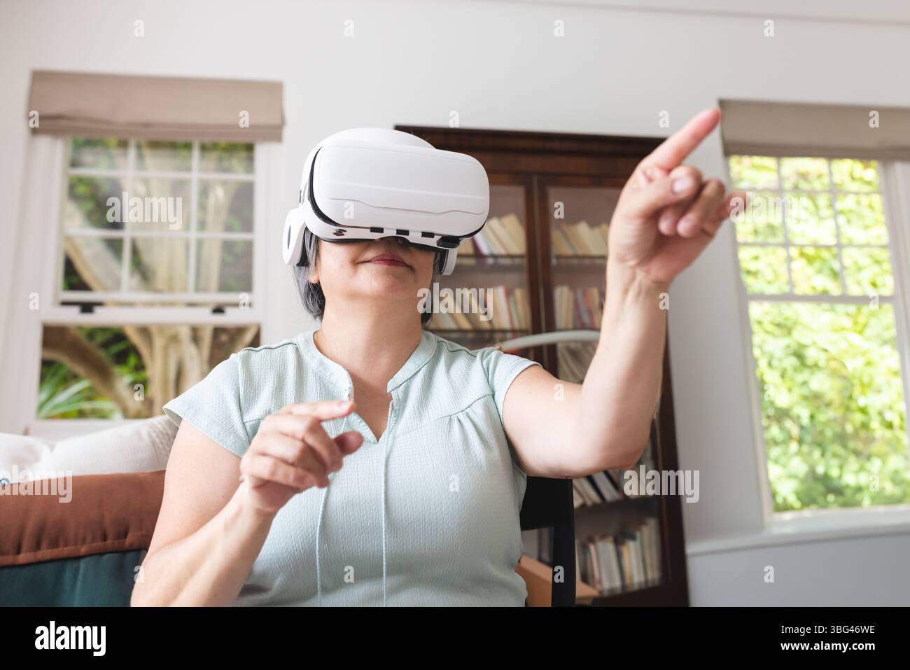 Woman is wearing white VR headset while leaning forward on sofa near ...