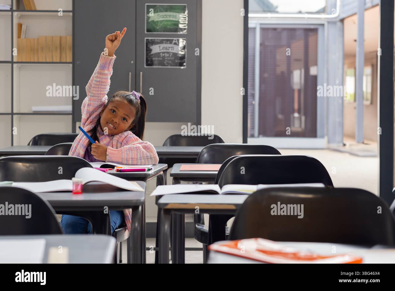 Female child student raising hand while writing in notebook at ...