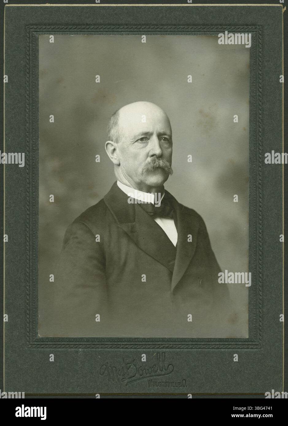 Studio portrait of a bald man with a mustache, dressed in a dark suit ...
