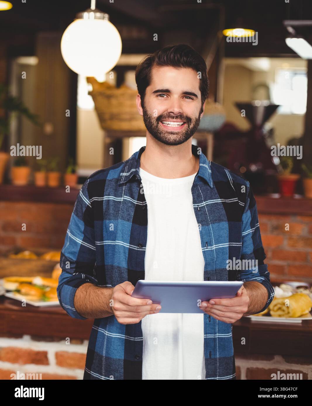 Smiling cafe manager holding tablet in bakery with counter displaying ...