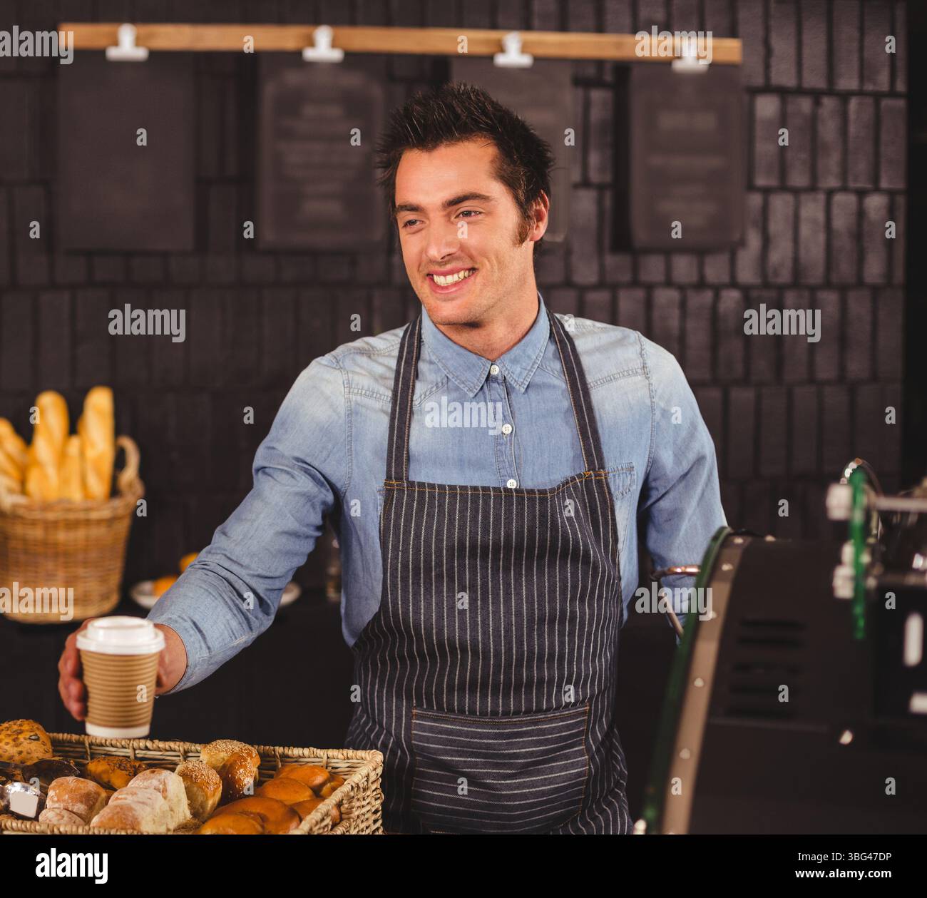 Male barista handing coffee cup forward behind bakery counter with ...