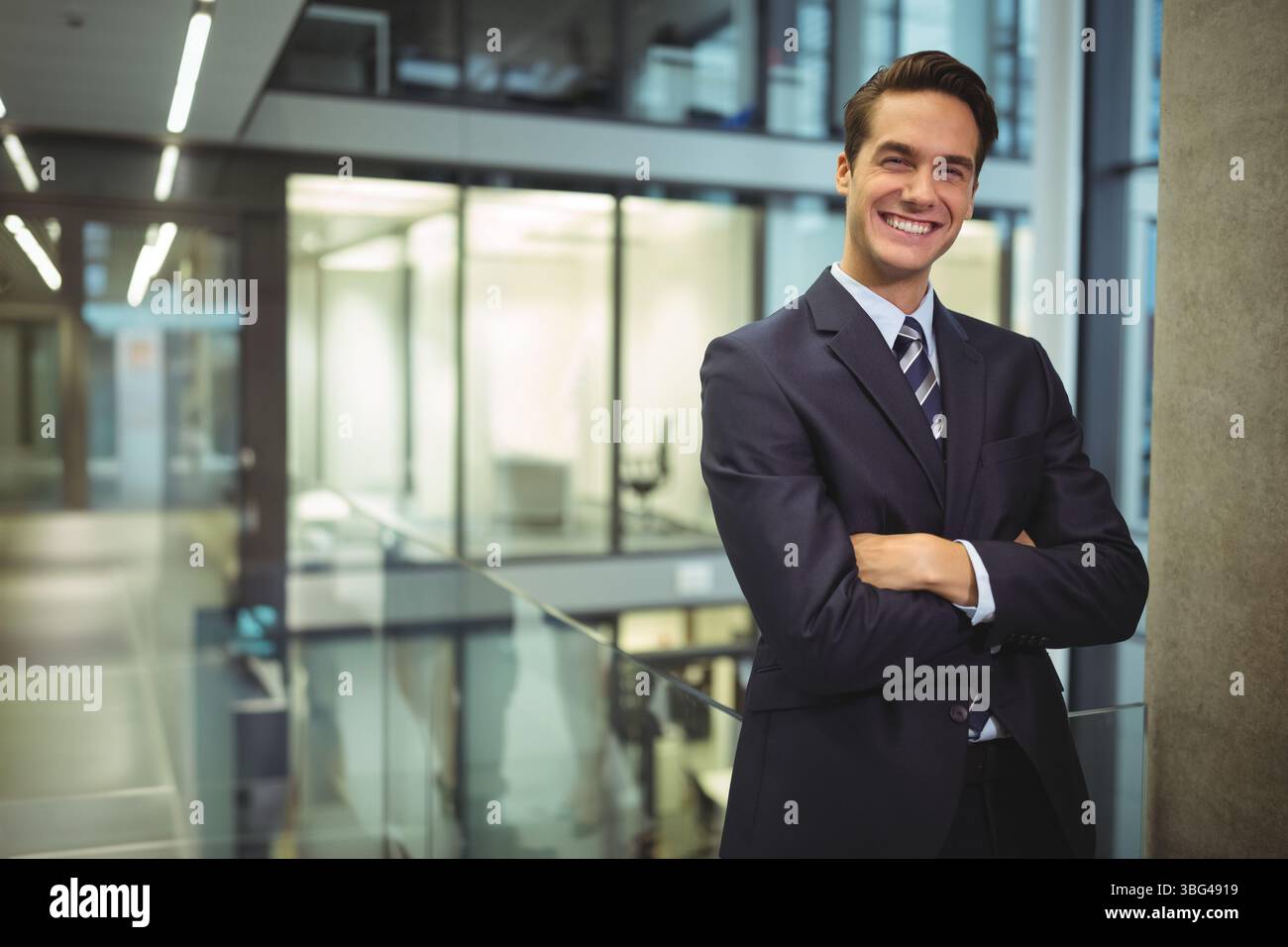 Man in suit leaning arms crossed against column at office atrium with ...