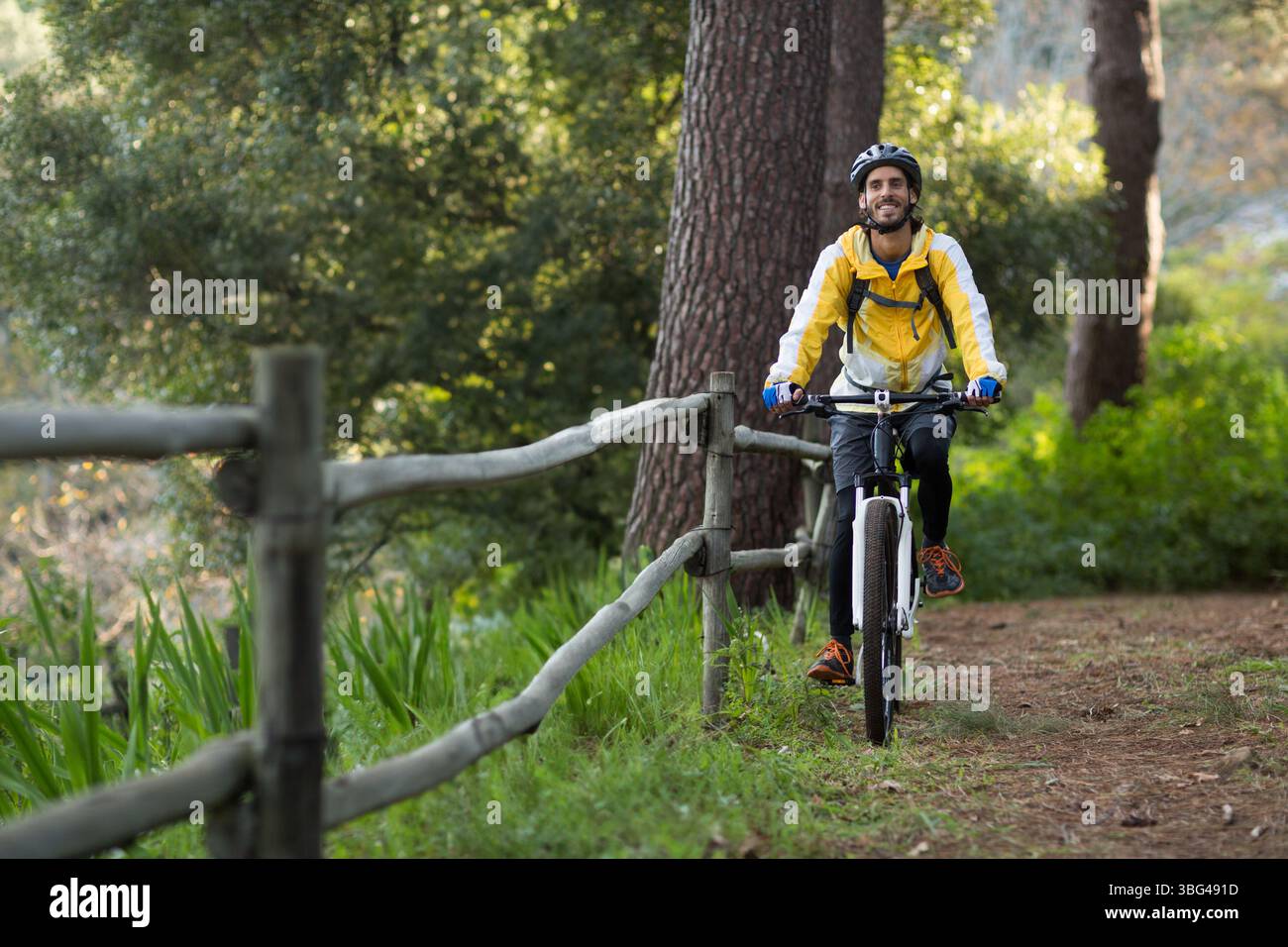 Man cycling on mountain bike wearing yellow jacket and helmet along wooded trail past wooden ...