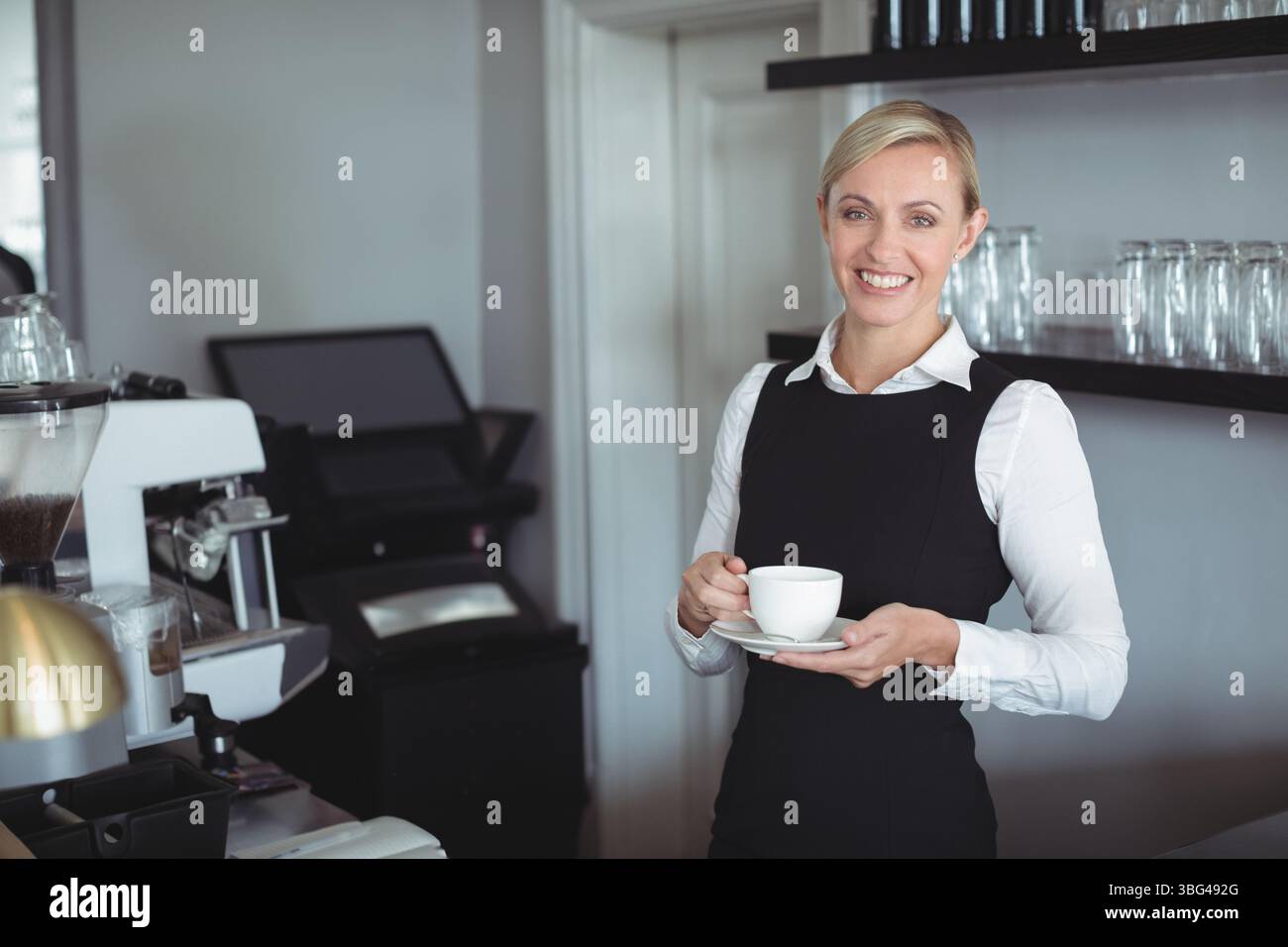 Female barista wearing black dress holding cup and saucer at cafe ...
