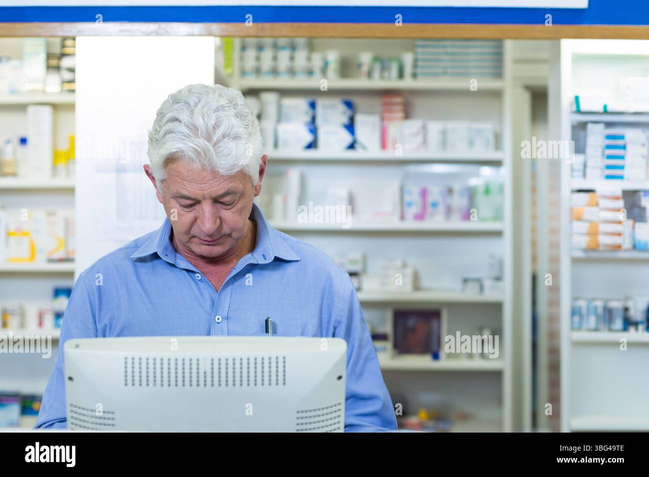 Senior male pharmacist in blue shirt checking white monitor at pharmacy ...