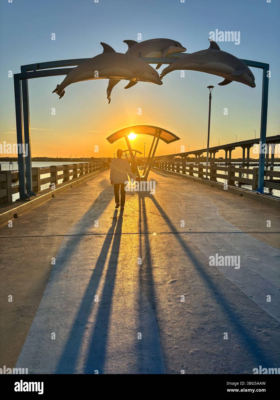 A person walks toward sunset under a dolphin sculpture arch on the ...