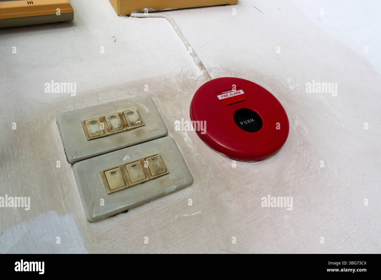 This image features a red emergency button set against a white wall ...